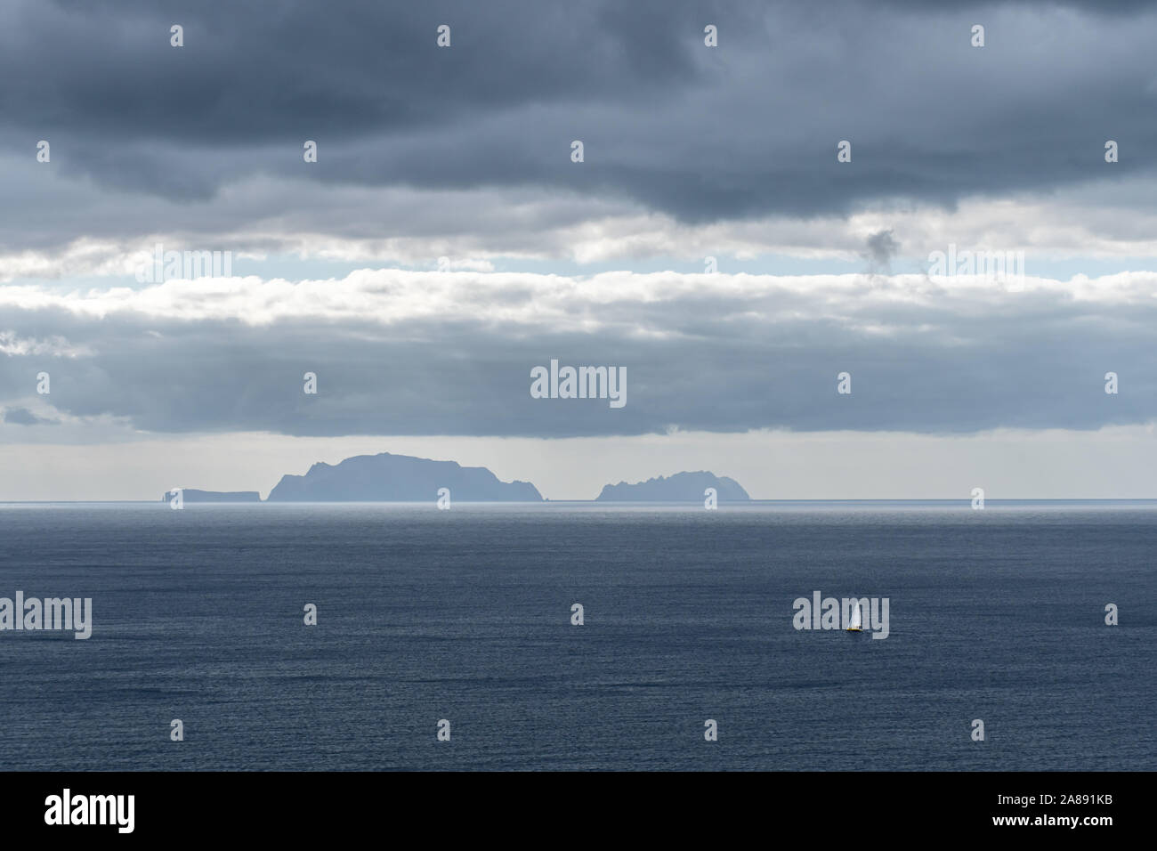 A small yacht sailing towards a distant island, sunbeams passing ...