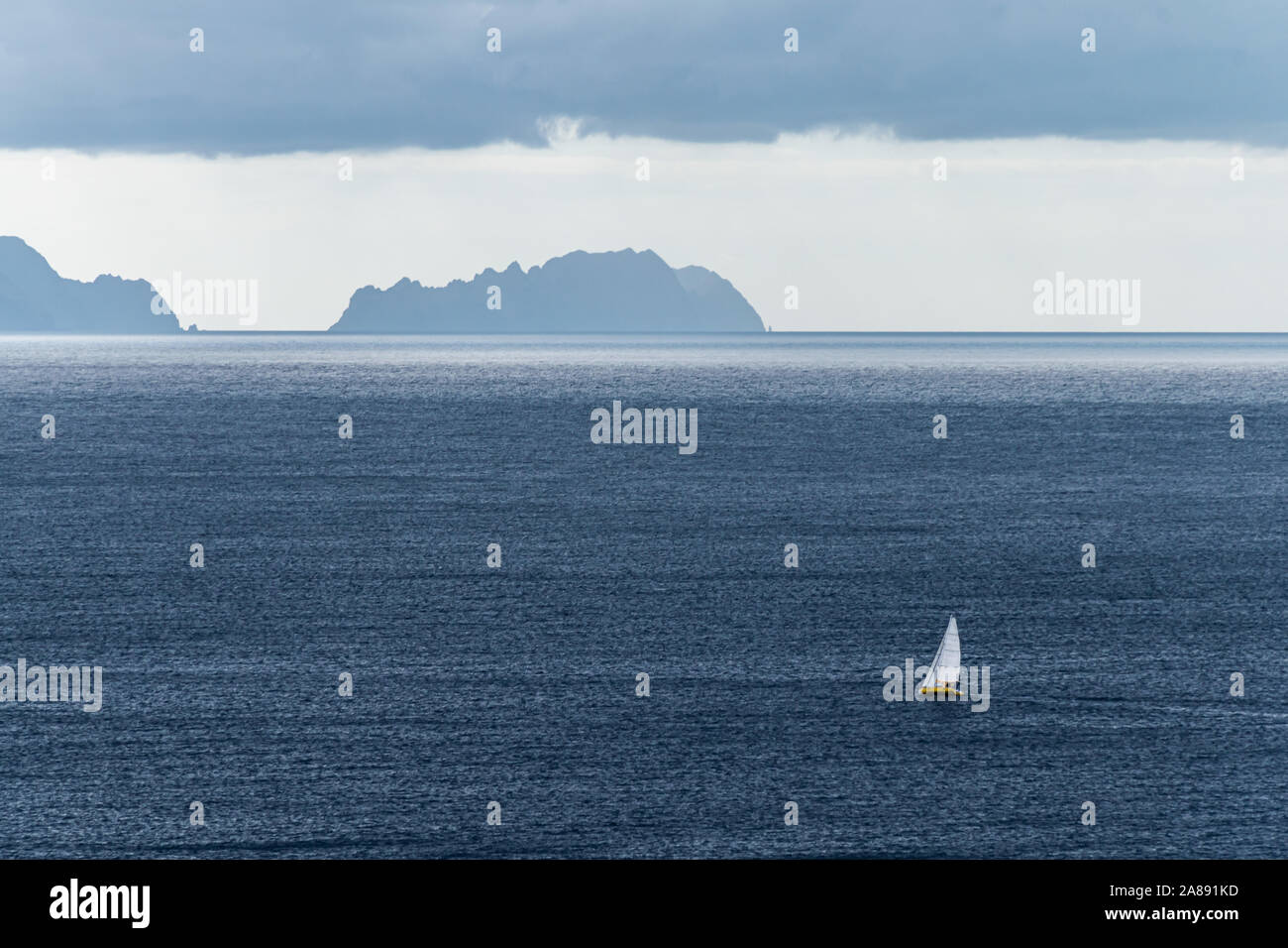 A small yacht sailing towards a distant island, sunbeams passing ...