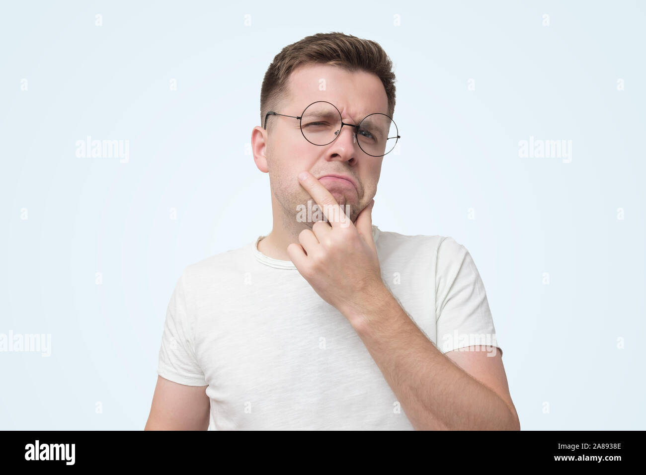 Serious male student in white t-shirt wears optical round glasses ...