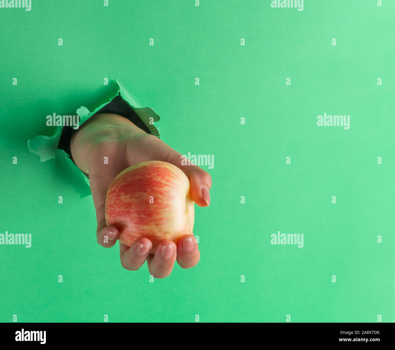 A woman holds an apple in her hand, inserted through a hole in torn ...