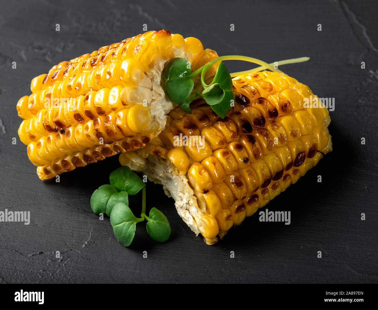 Grilled, delicious, yellow corn on the cob with green sprouts on a ...