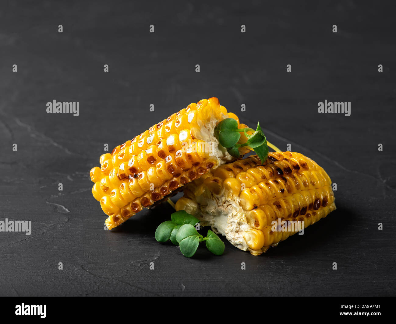 Grilled, tasty, yellow corn on the cob with green sprouts on a black ...