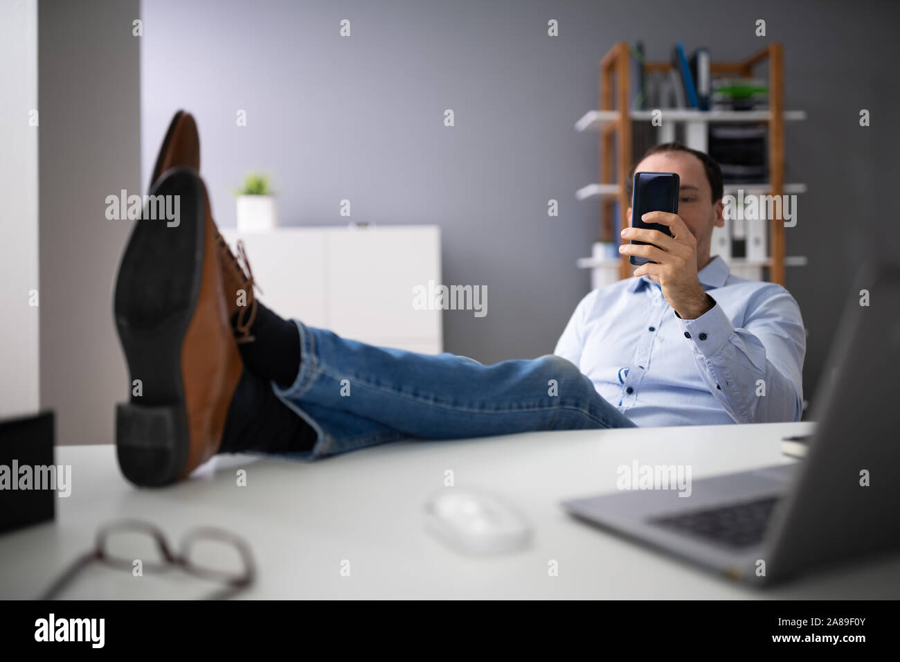 Lazy Man Using Phone At Work Desk Instead Of Working Stock Photo - Alamy