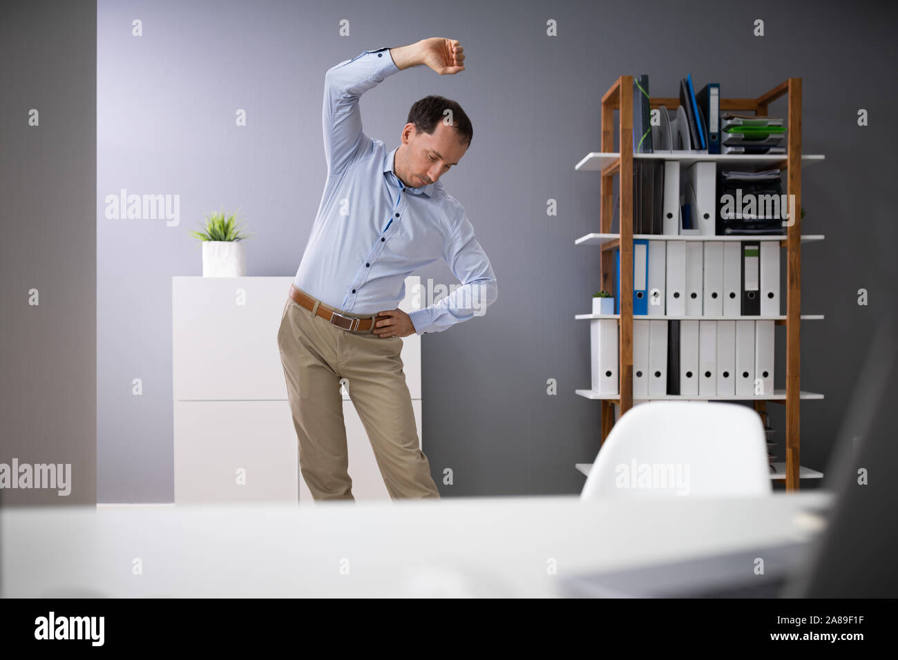 Portrait Of A Young Businessman Stretching In Office Stock Photo - Alamy