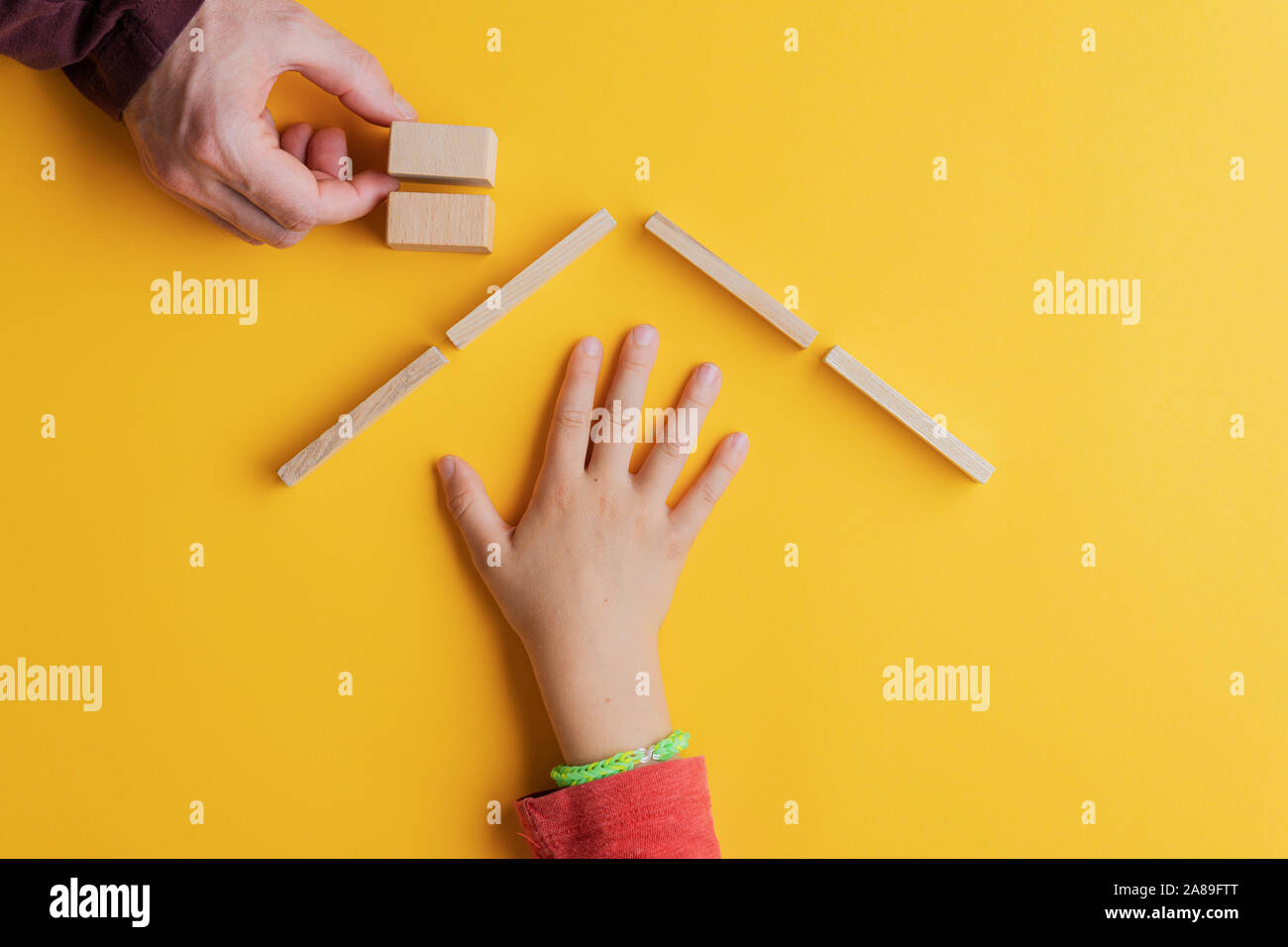 Male hand building a house of wooden pegs and cubes for a child hand to ...