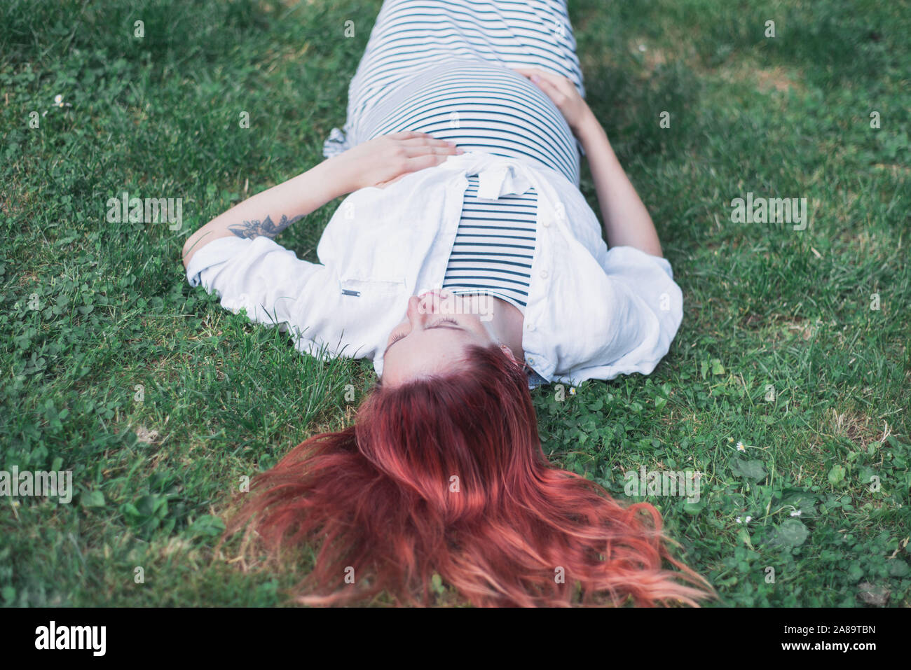 Pregnant White Girl Lies On Green Grass In A Light Striped Dress On A