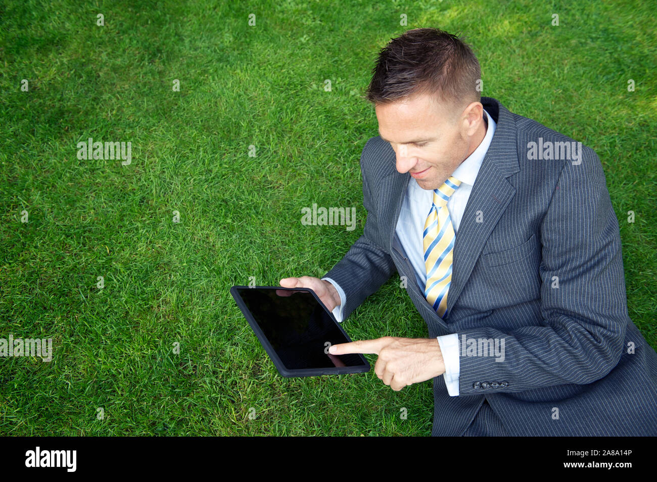 Young businessman reclining on green grass lawn using his tablet ...
