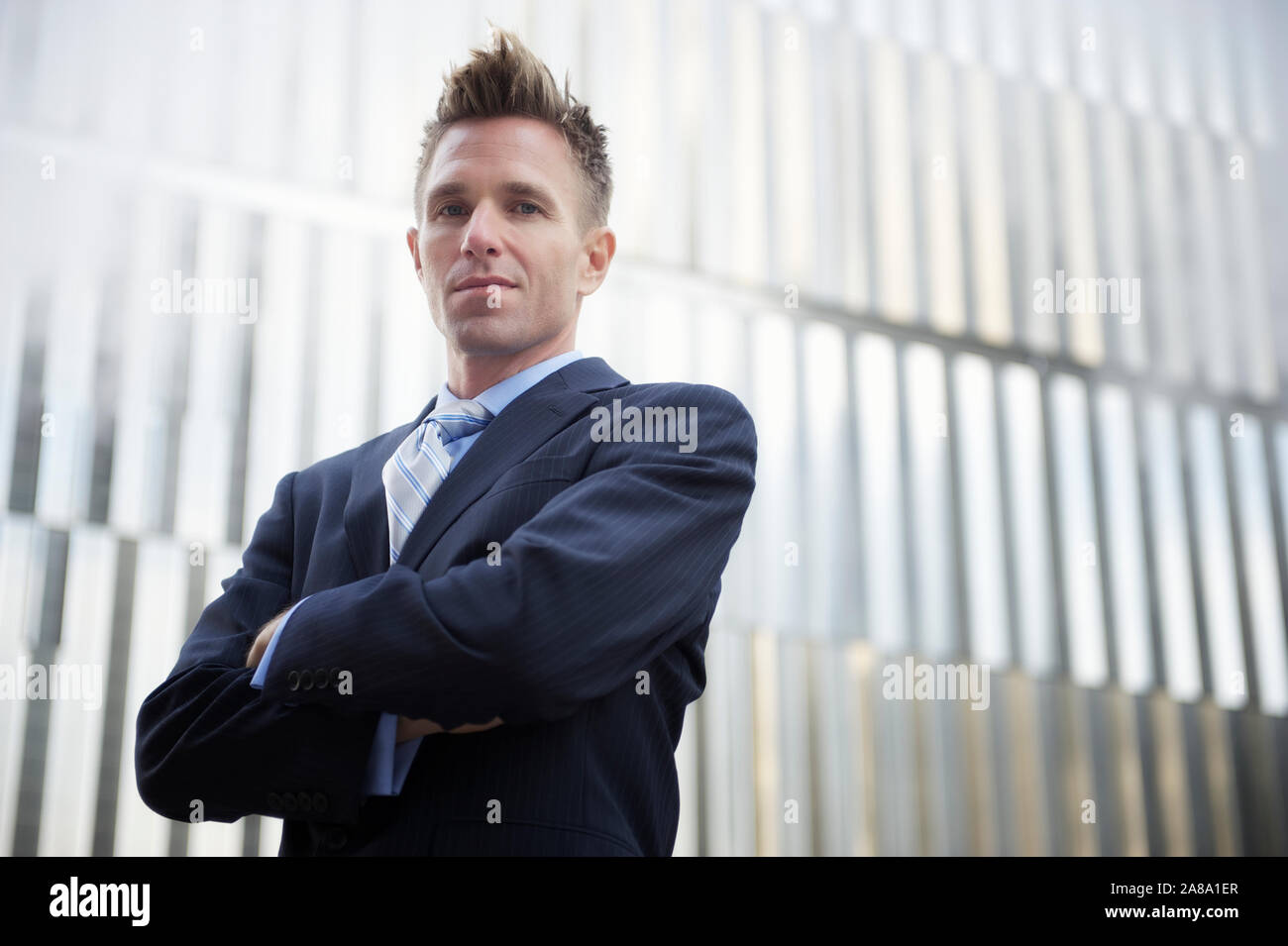 Young businessman with funky hair style standing with arms crossed in ...