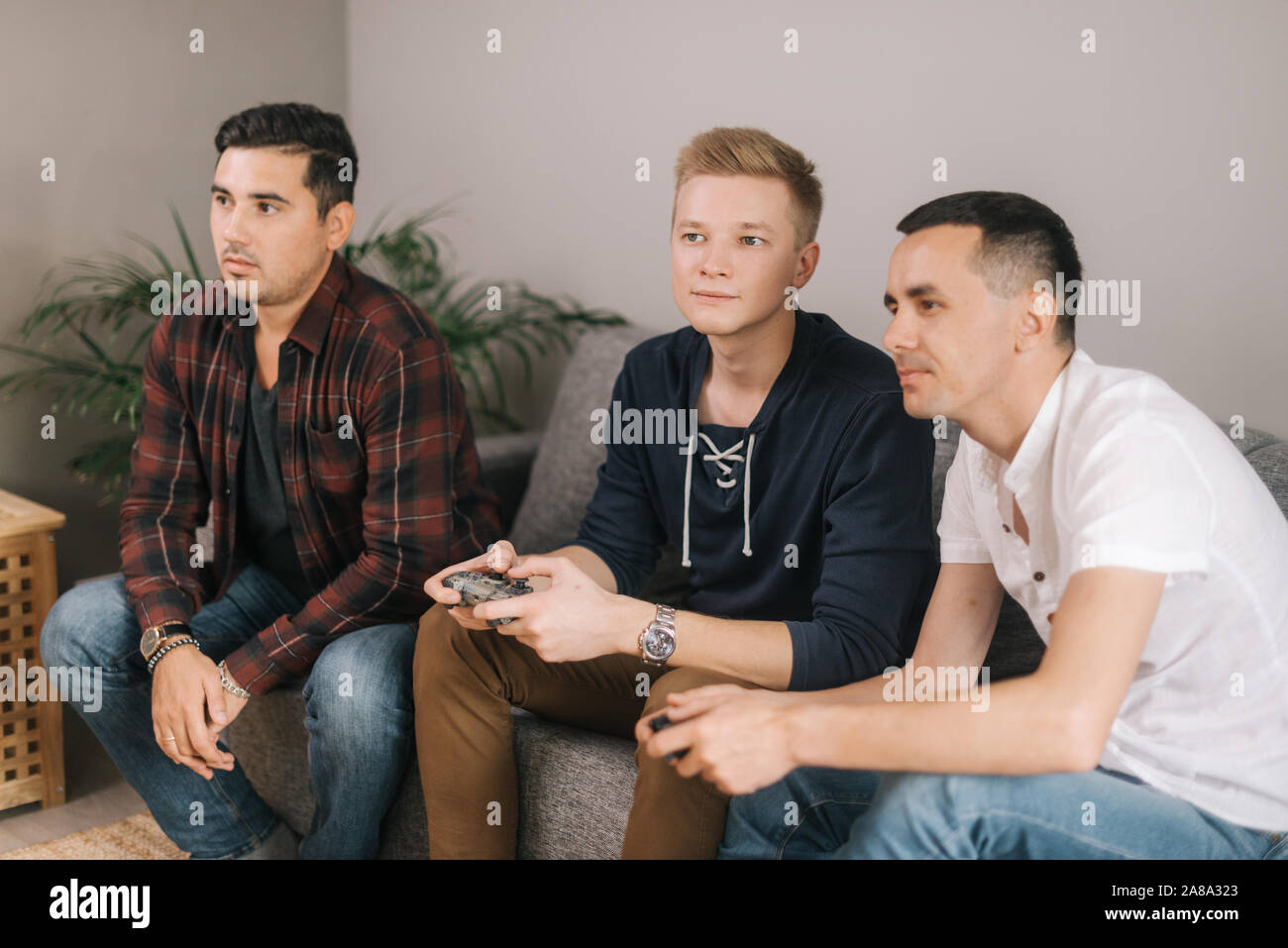 Three cheerful young guys are sitting in the living room and play game ...
