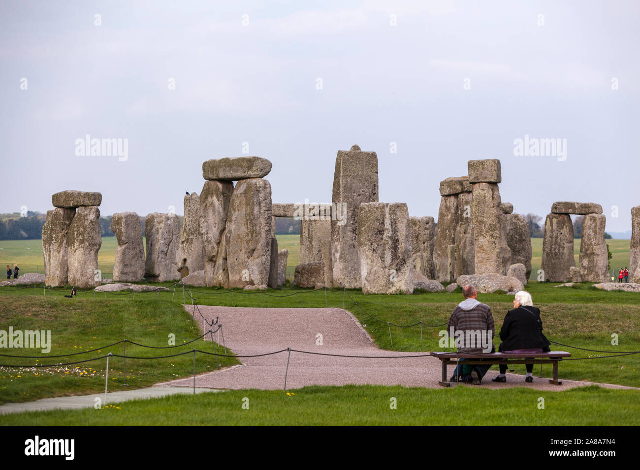 Old couple seated looking Stonehenge, a ring of standing stones ...
