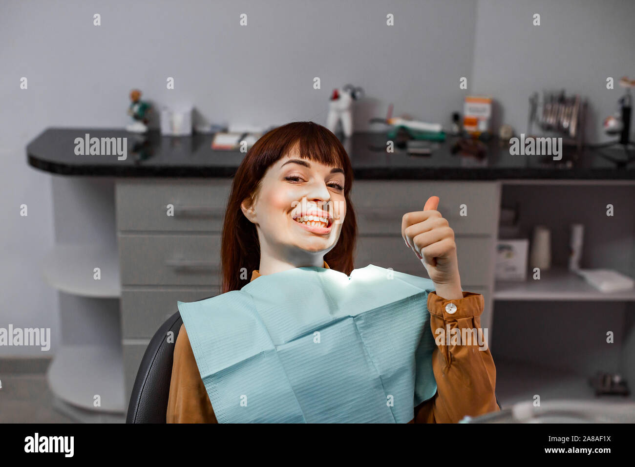 Happy young smiling woman showing thumb up sitting at the dentist ...