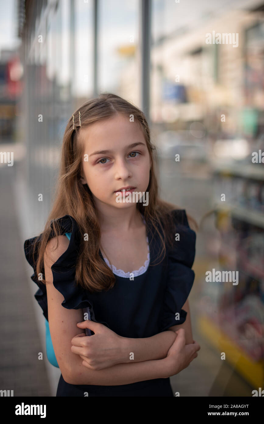 Schoolgirl in a blue dress posing on the street. A girl with blond hair ...