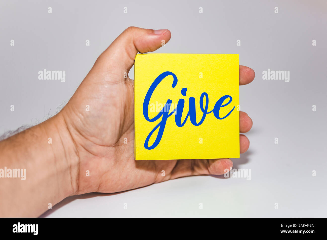 man hand holding a yellow note paper with the text give against white ...