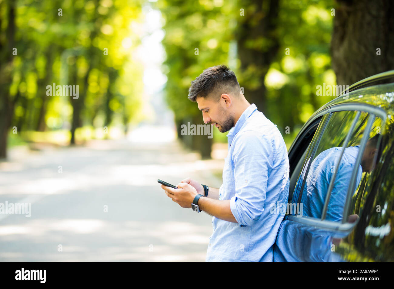 Successful man standing by his car texting on mobile phone Stock Photo ...