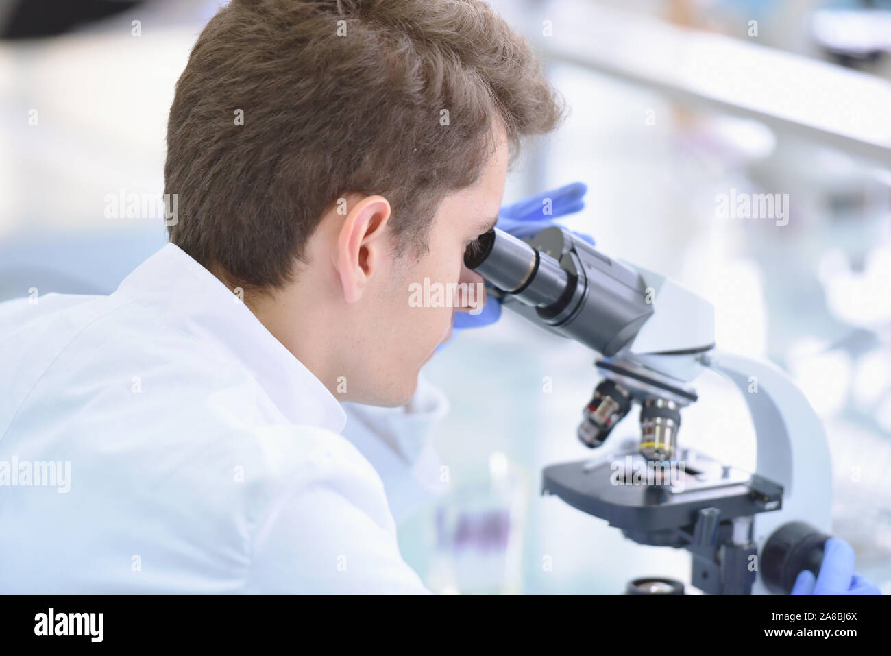 Young male scientist looking through a microscope in a laboratory doing ...