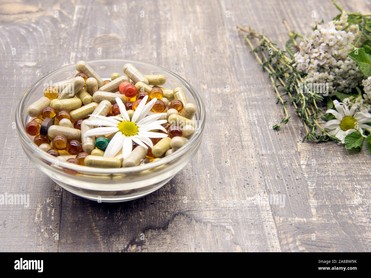 A bowl with various capsules and tablets, medicinal and aromatic herbs ...