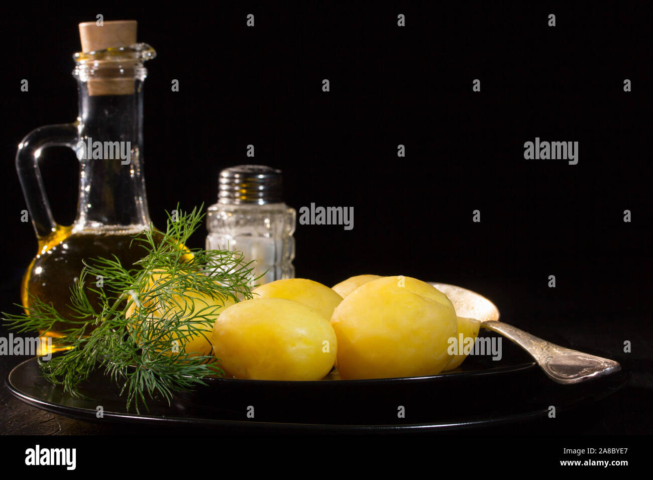 Boiled potatoes, dill, vegetable oil and salt on a dark background ...