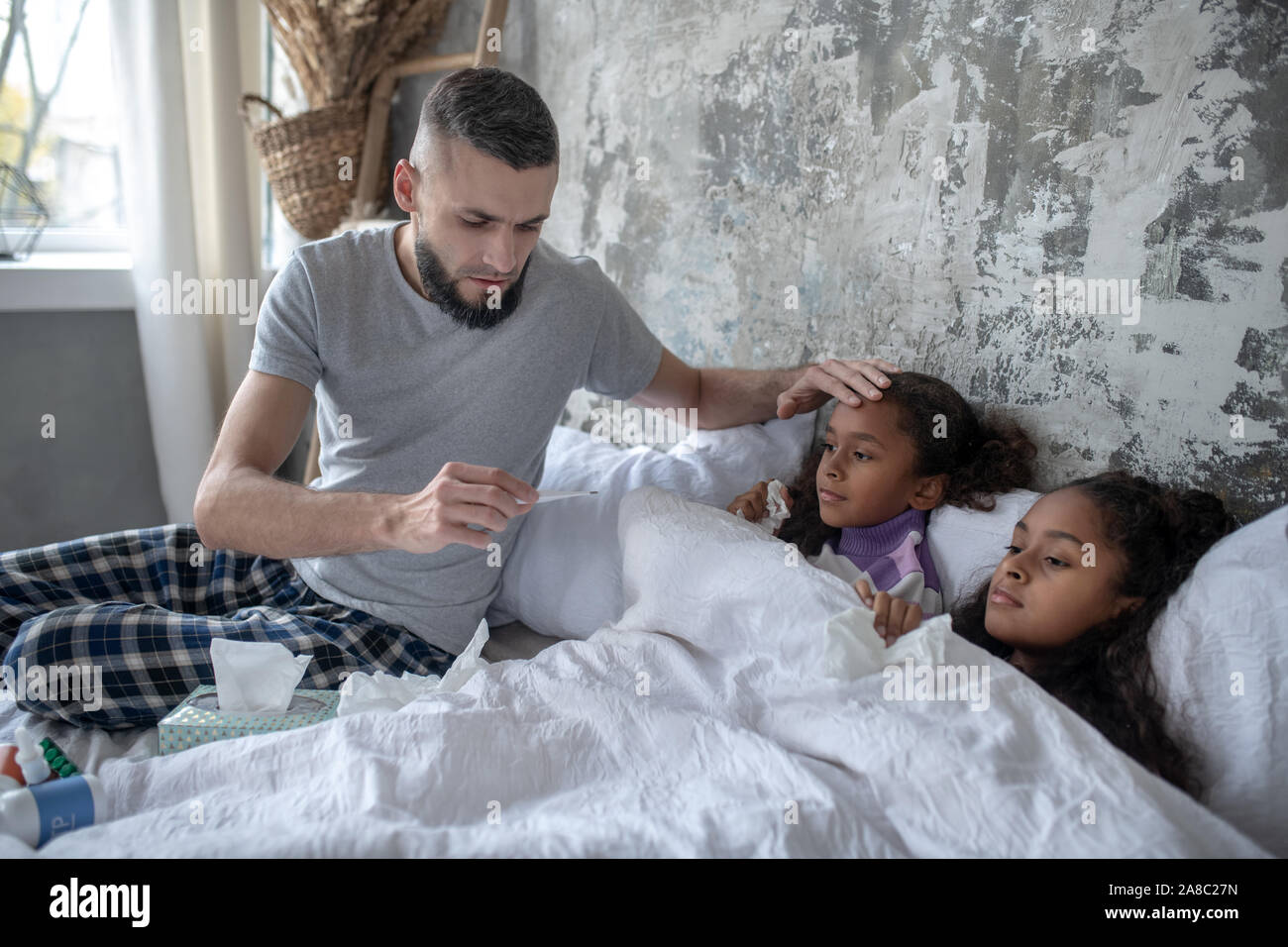 Sick daughters lying in bed while father measuring temperature Stock ...