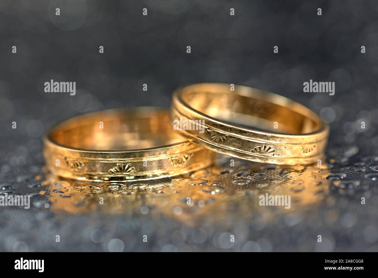 Two golden wedding rings in front of dark background Stock Photo - Alamy