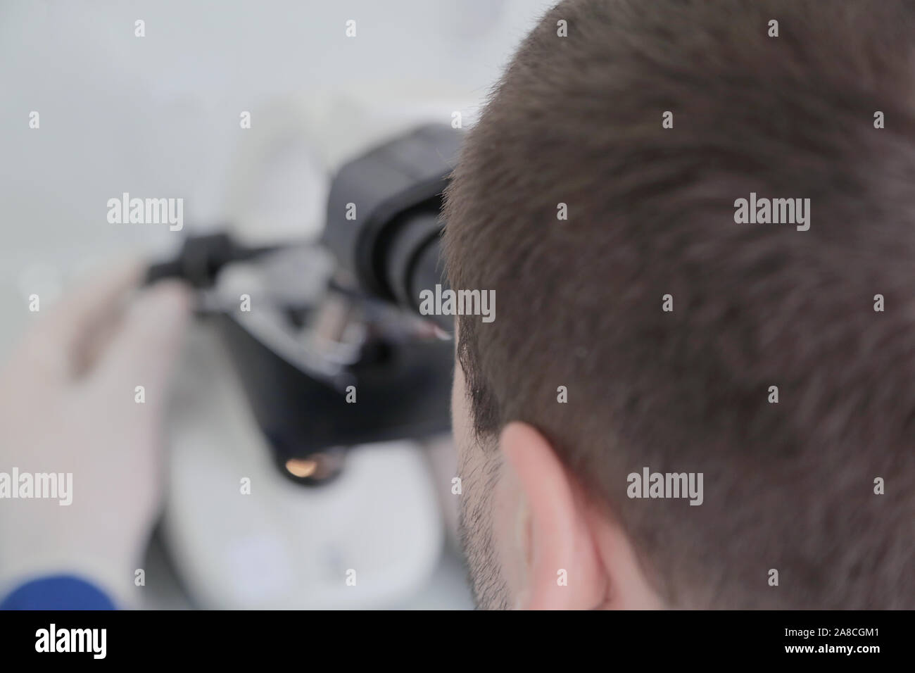 Young male male scientist looking through a microscope in a laboratory ...