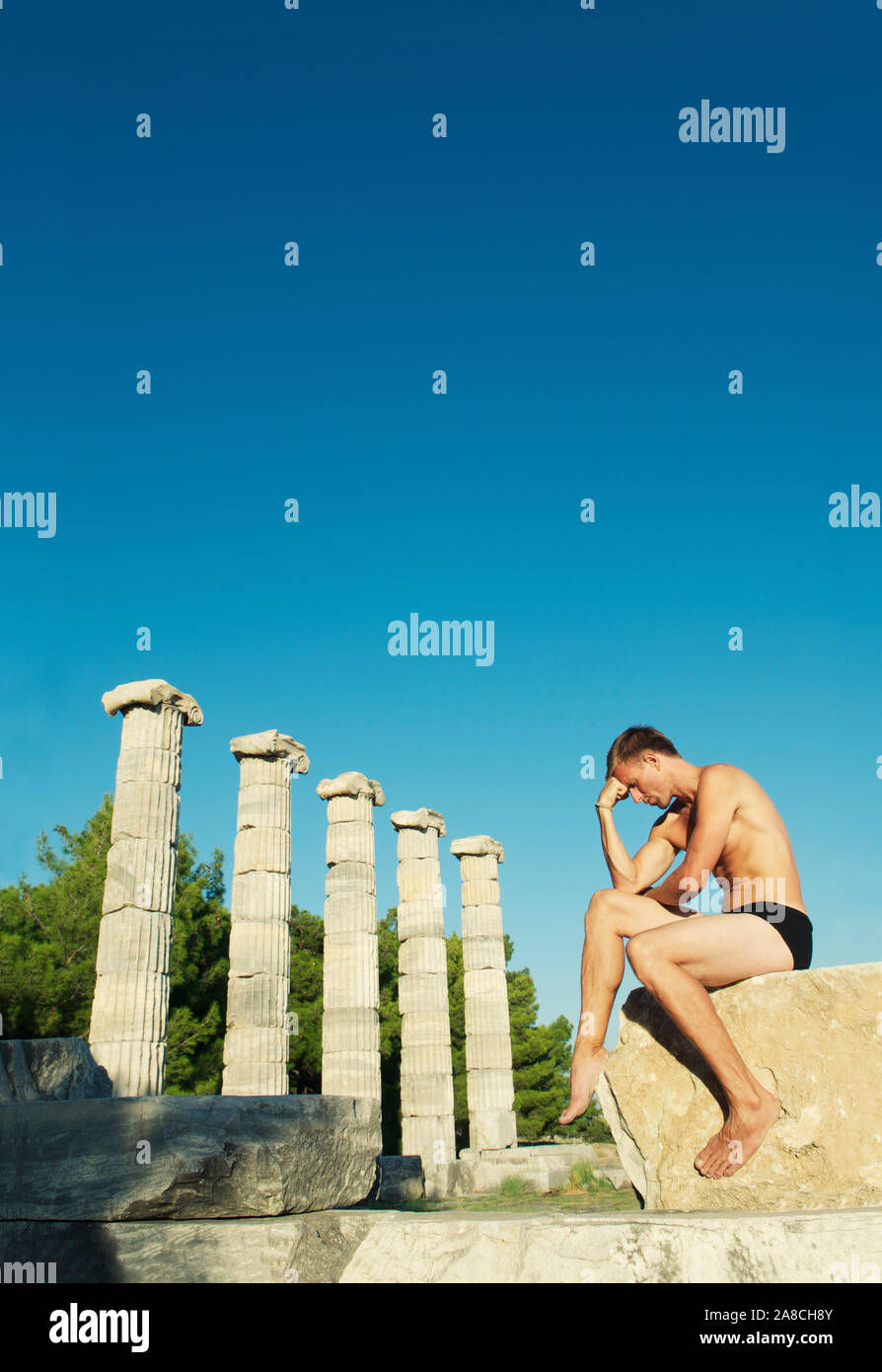 Man sitting in classic thinker pose on a stone pedestal next to row of ...