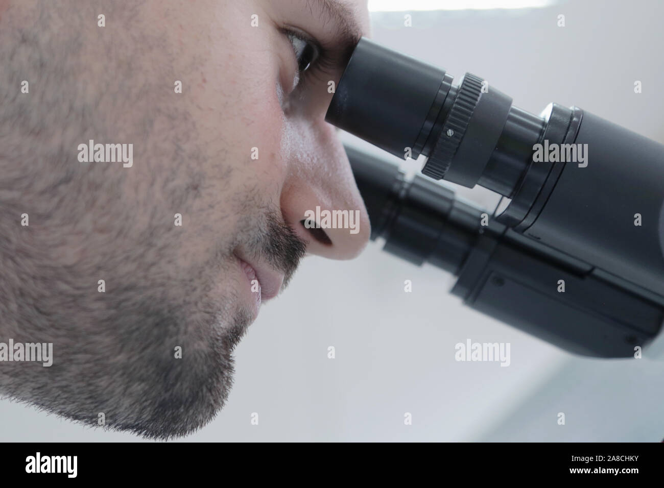 Young male male scientist looking through a microscope in a laboratory ...