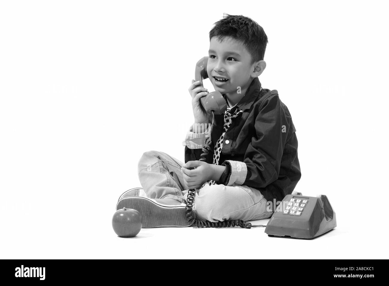 Studio shot of cute happy boy smiling and talking on old telephone ...