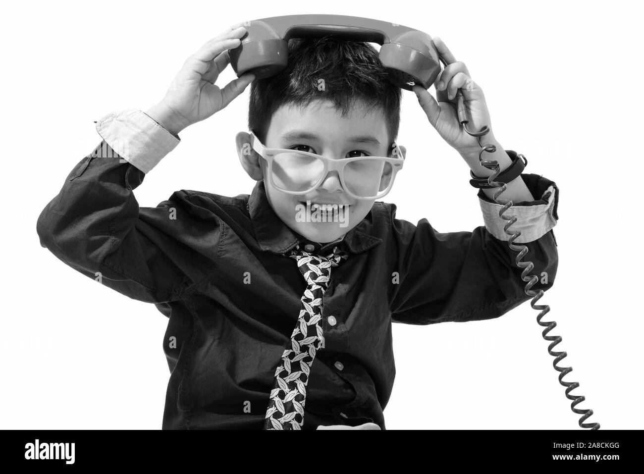Studio shot of cute happy boy smiling and putting old telephone on head ...