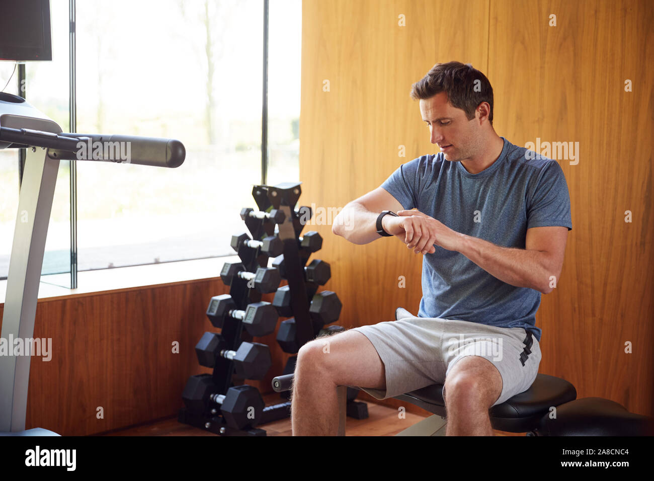Man Exercising Sitting On Weight Bench In Home Gym Checking Smart Watch ...