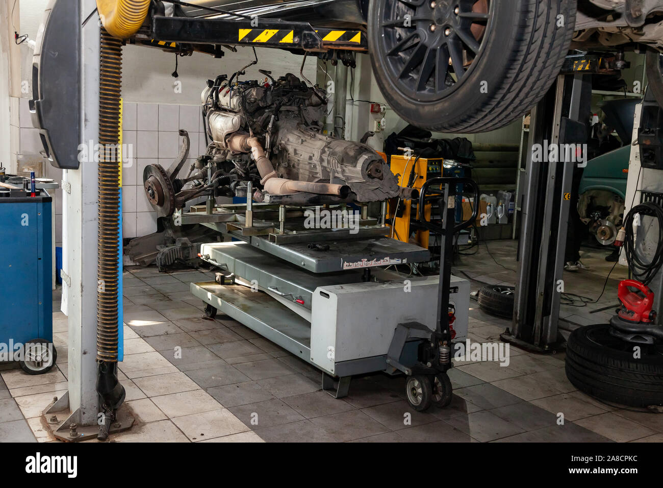 A used car raised on a lift for repair and under it a detached engine ...