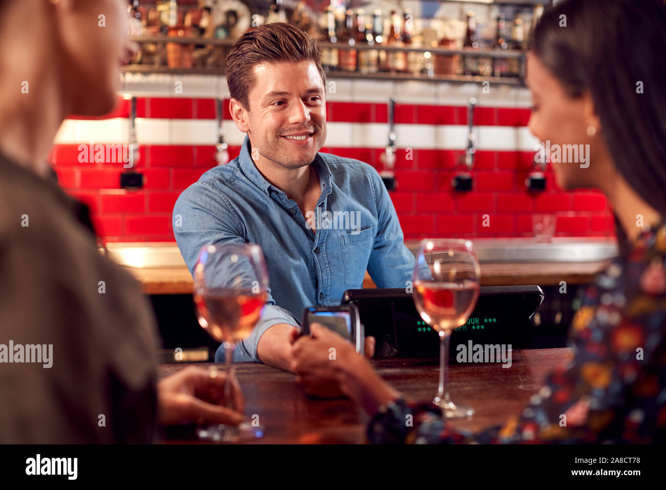 Woman Paying Barman For Drinks At Bar After Work Using Contactless Card ...