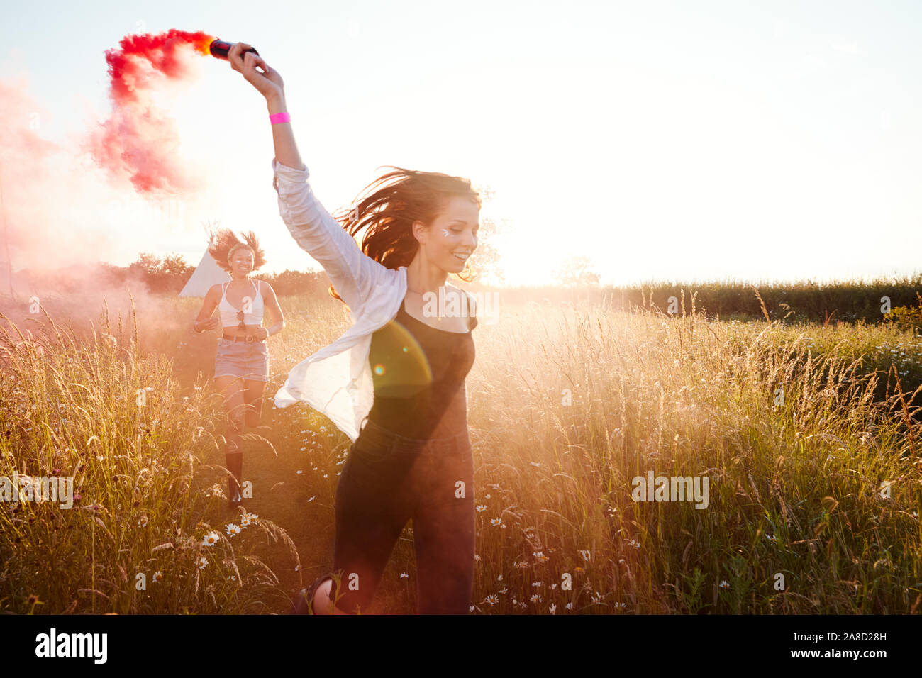 Two Female Friends Camping At Music Festival Running Through Field With ...