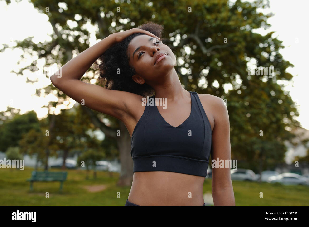 Portrait of a fit young black woman stretching her neck in the park ...