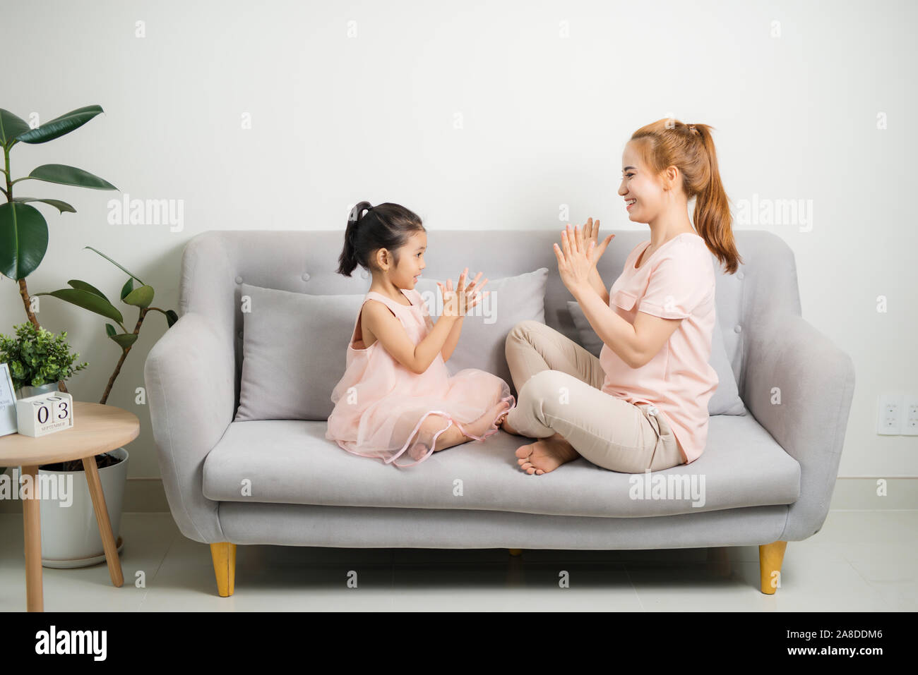 Side view portrait of little girl playing clapping game with mom sitting on sofa together Stock ...