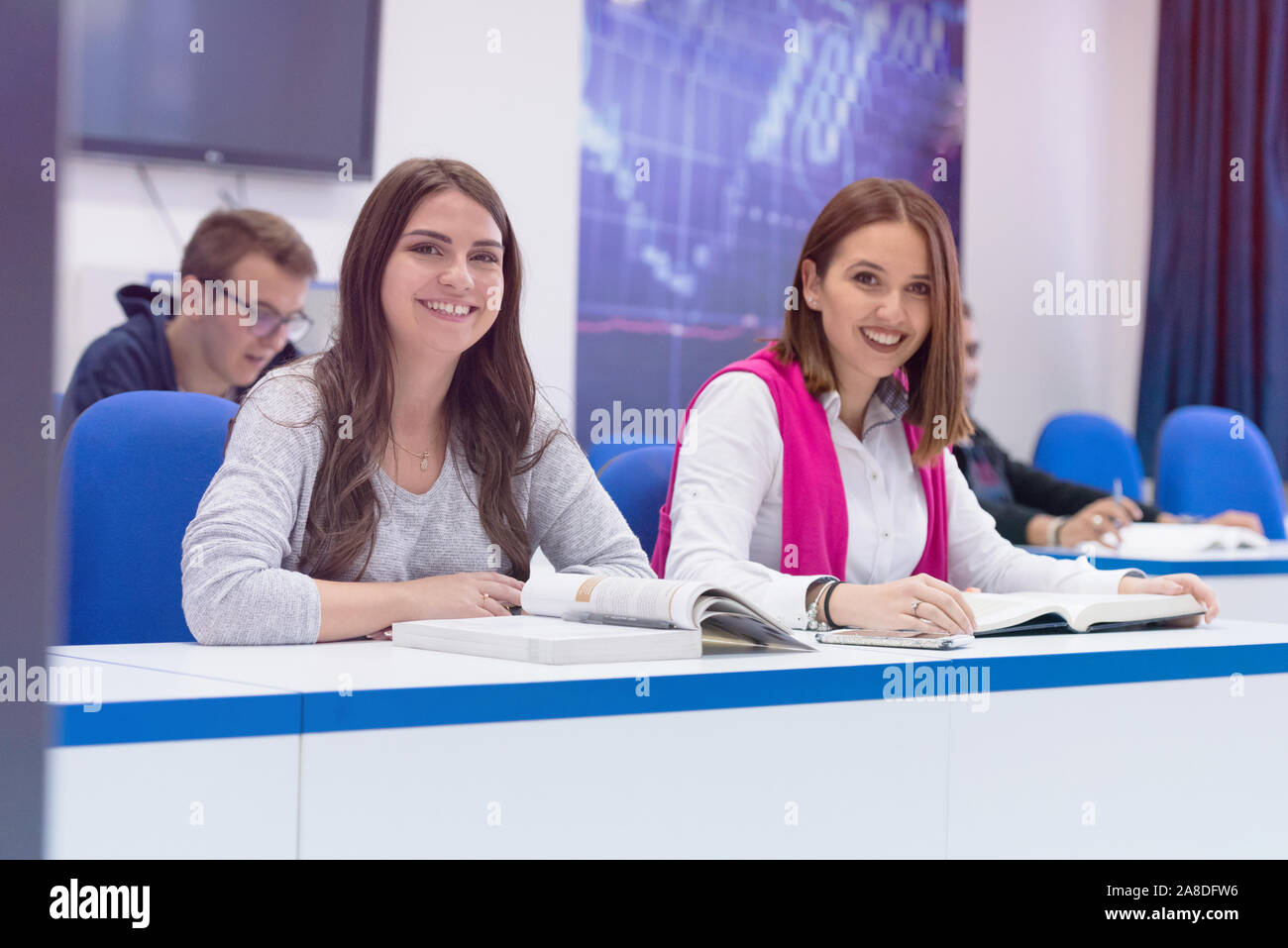 Two university female students in class sits at their desk turning to ...