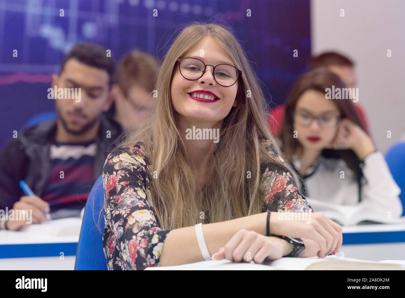 University female student in class sits at her desk turning to smile at ...