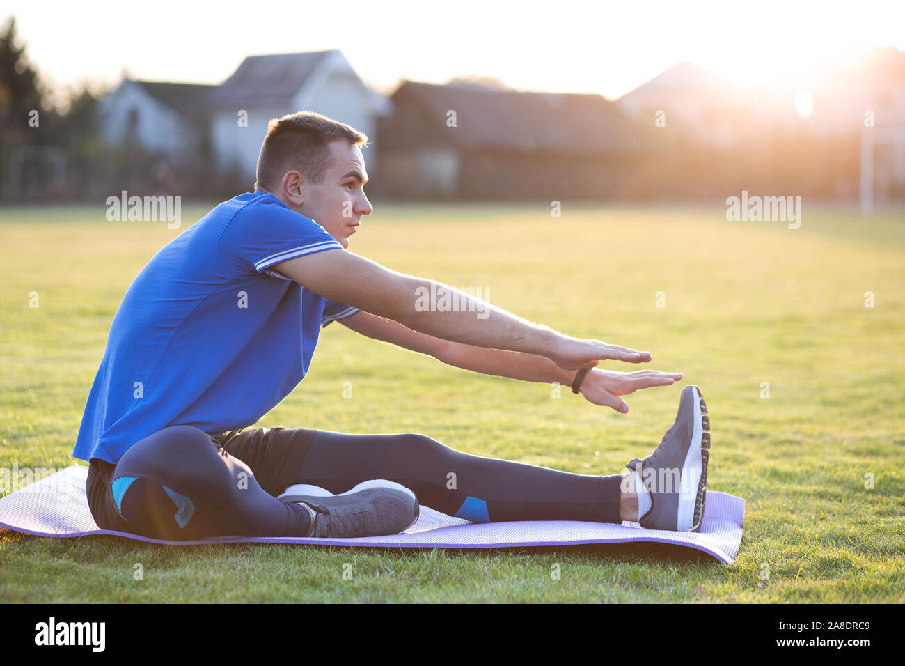 Young sportive man doing stretching exercises before running in morning ...