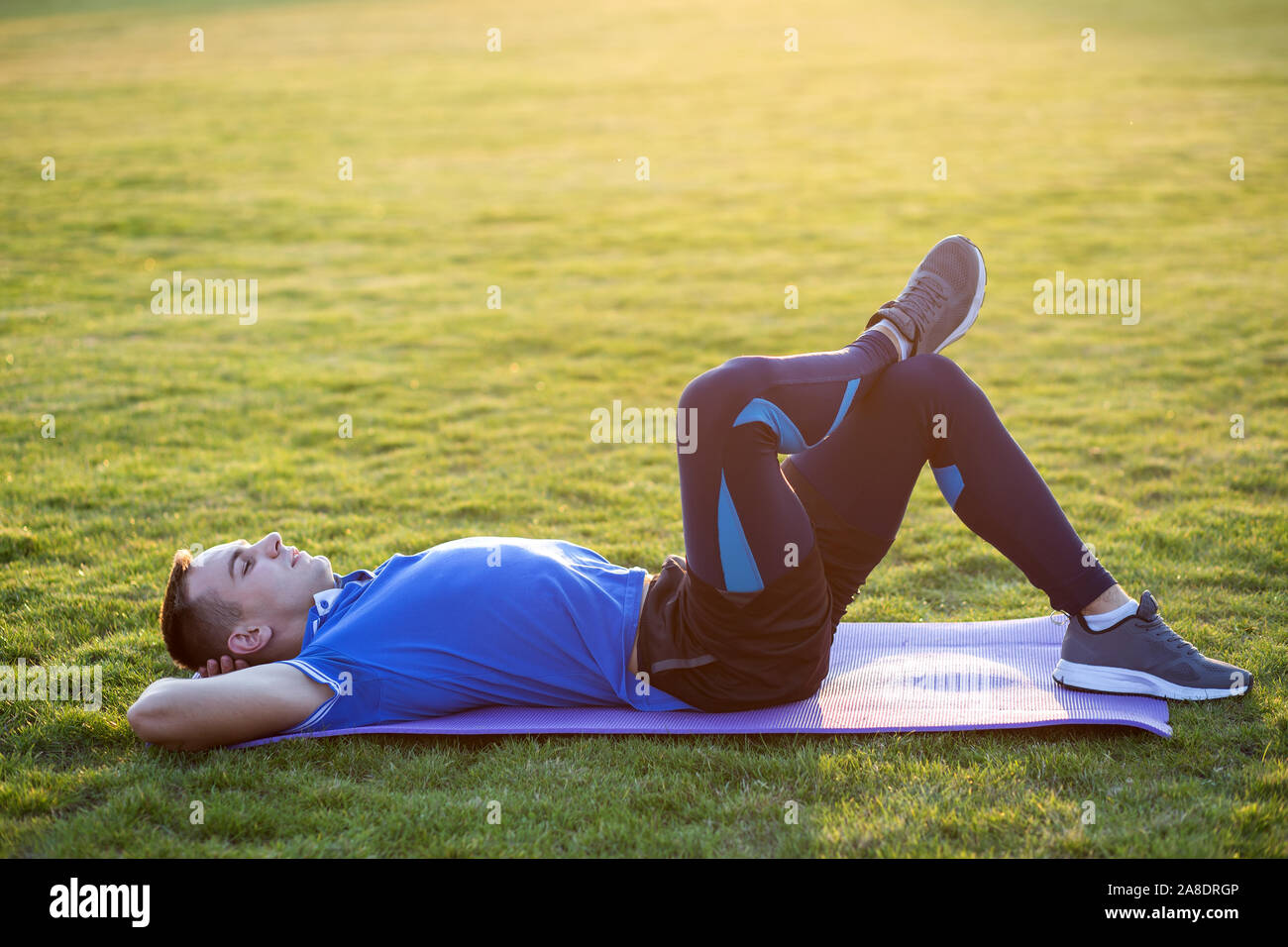 Young sportive man laying on training mat in morning field outdoors ...