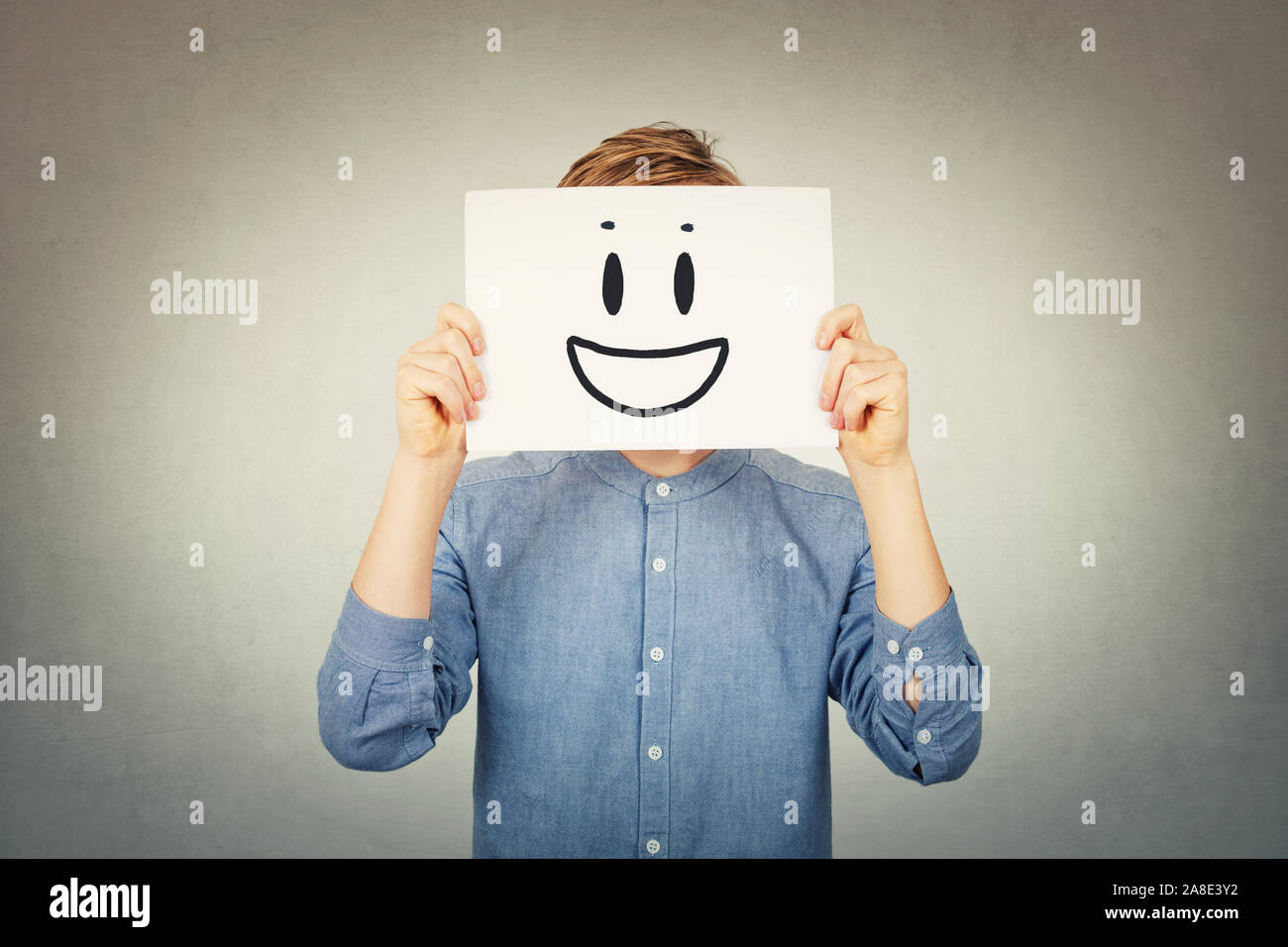Teenage guy covering face using a white paper sheet with smiling ...