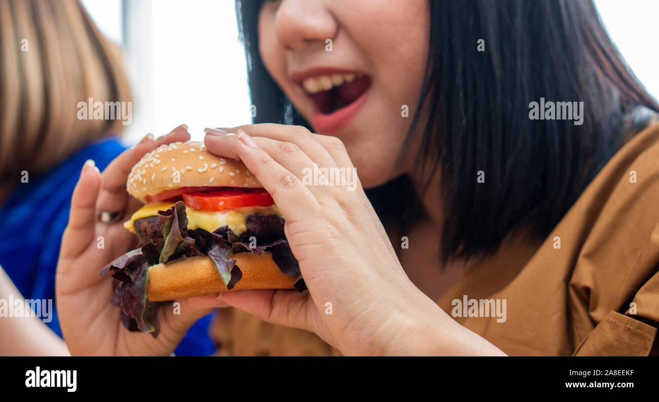 Hungry overweight woman smiling and holding hamburger and sitting in ...