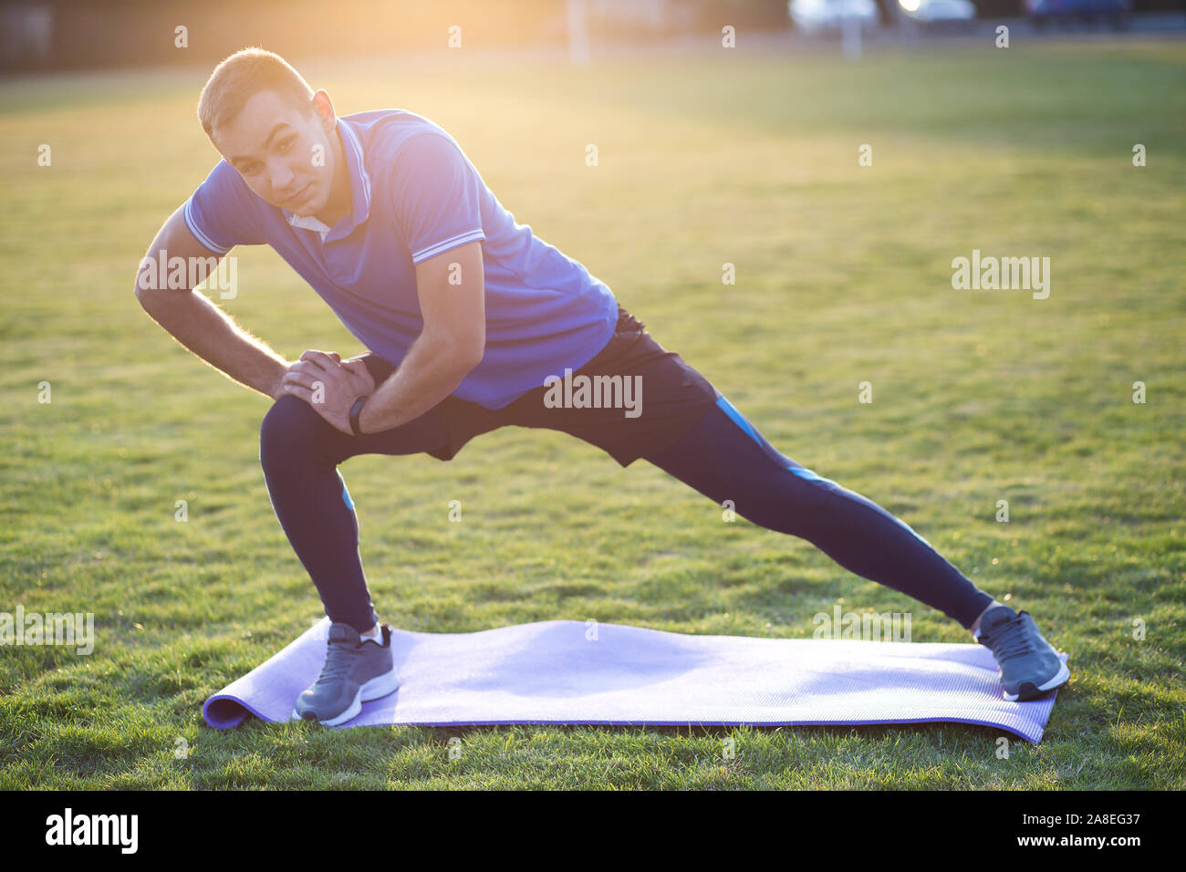 Young sportive man doing stretching exercises before running in morning ...