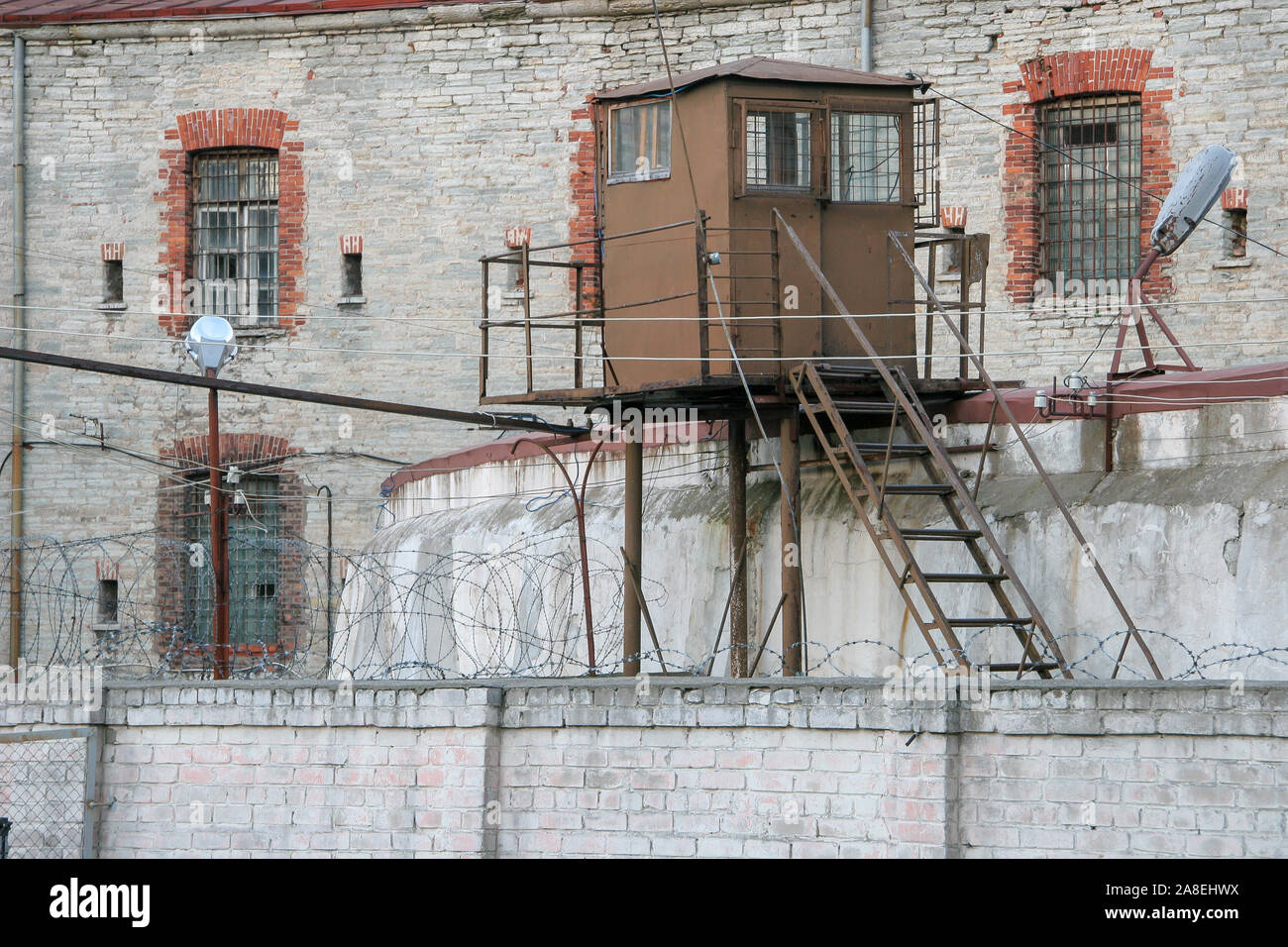 Old prison wall with barbed wire and observation tower behind it. Light ...