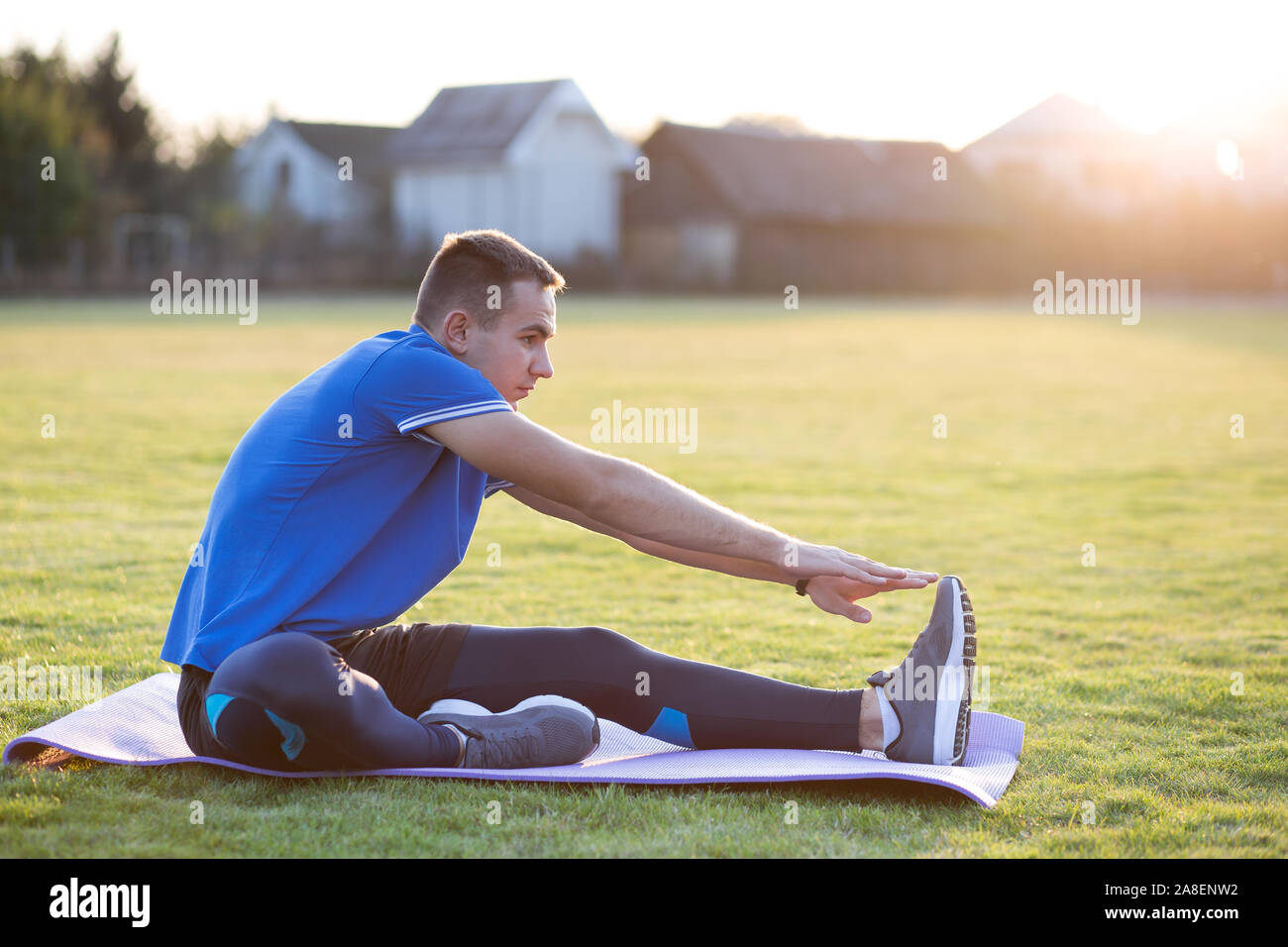 Young sportive man doing stretching exercises before running in morning ...