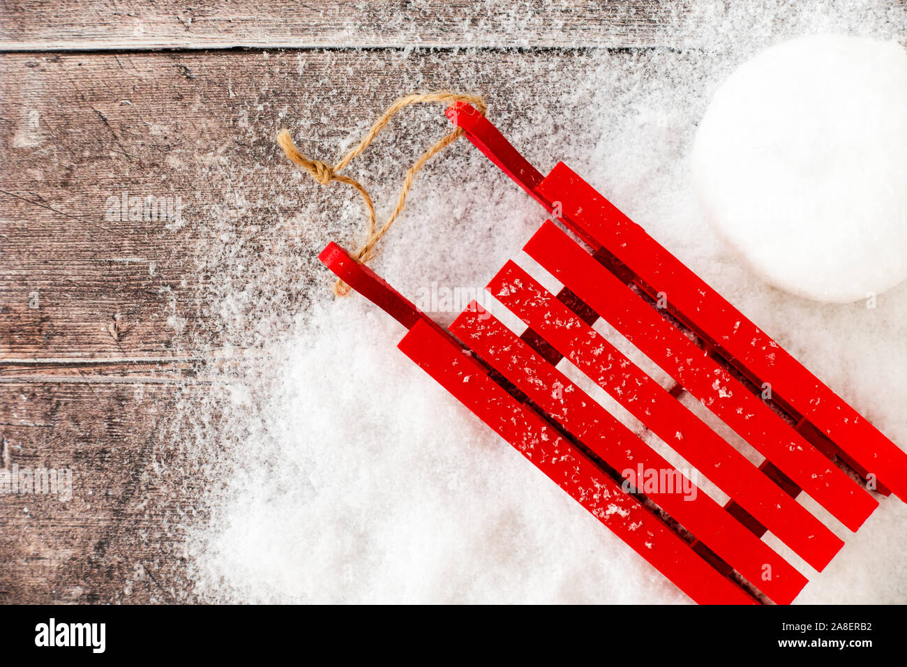 Red sledge and a snowball in snow and on brown rustic wood panel ...