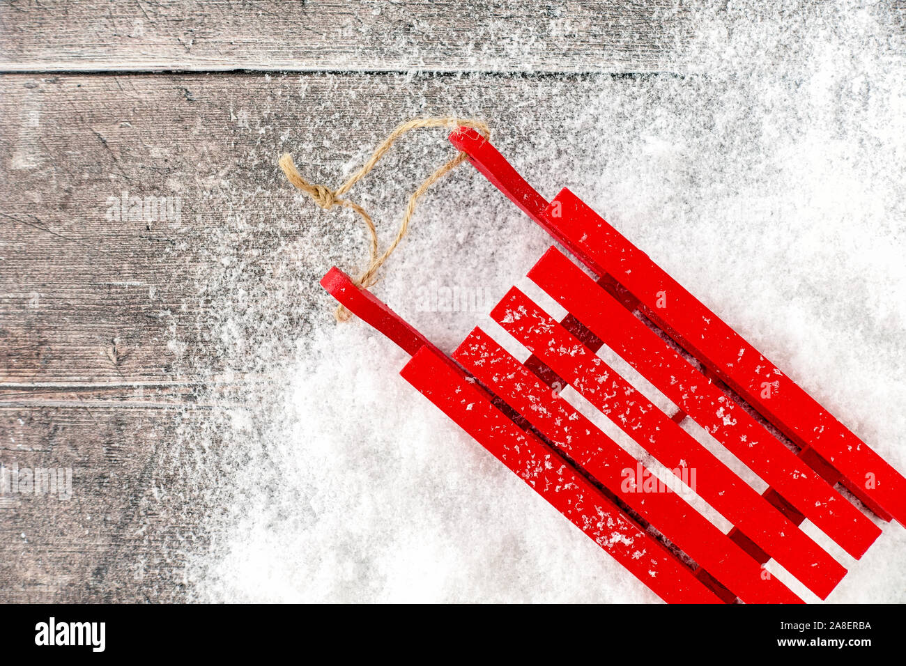 Red sledge covered with snowflakes in snow and on brown rustic wood ...