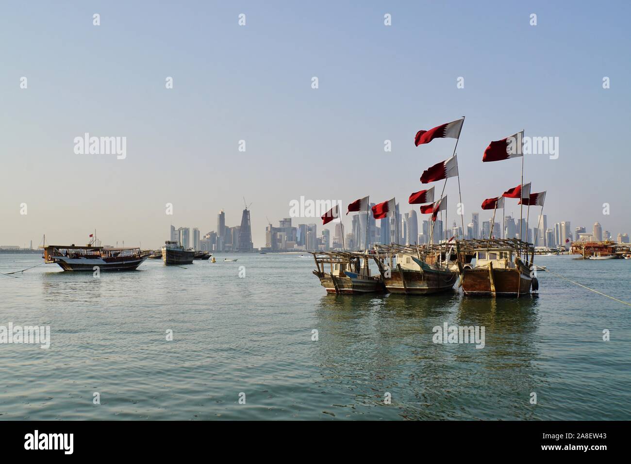 View of the skyline of Doha with traditional boats and flags in front ...