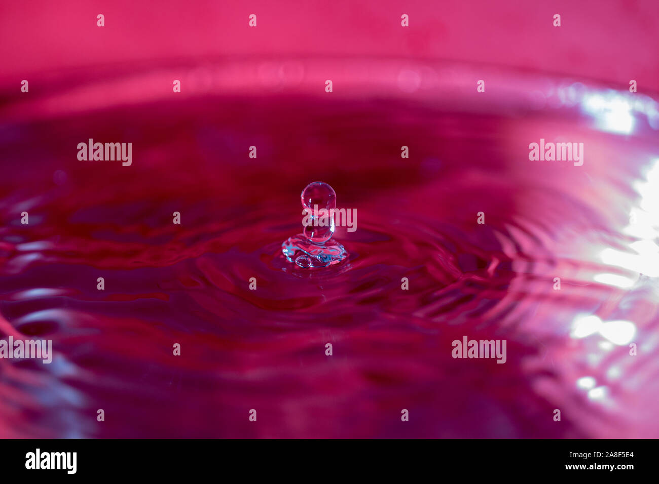 water drop splash in a red colored glass Stock Photo - Alamy