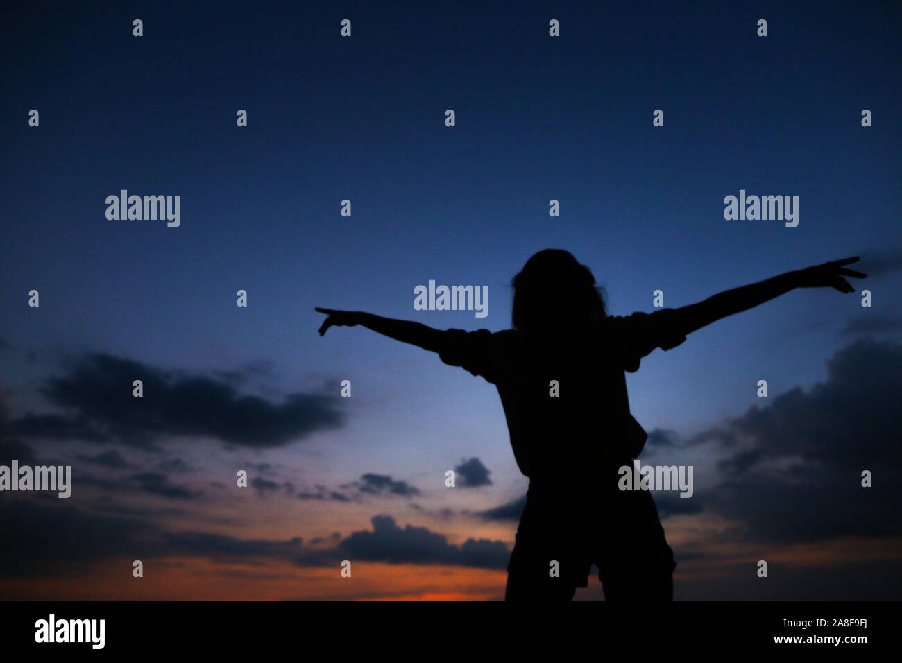 Black silhouette of young woman in sunset dark blue sky with clouds ...