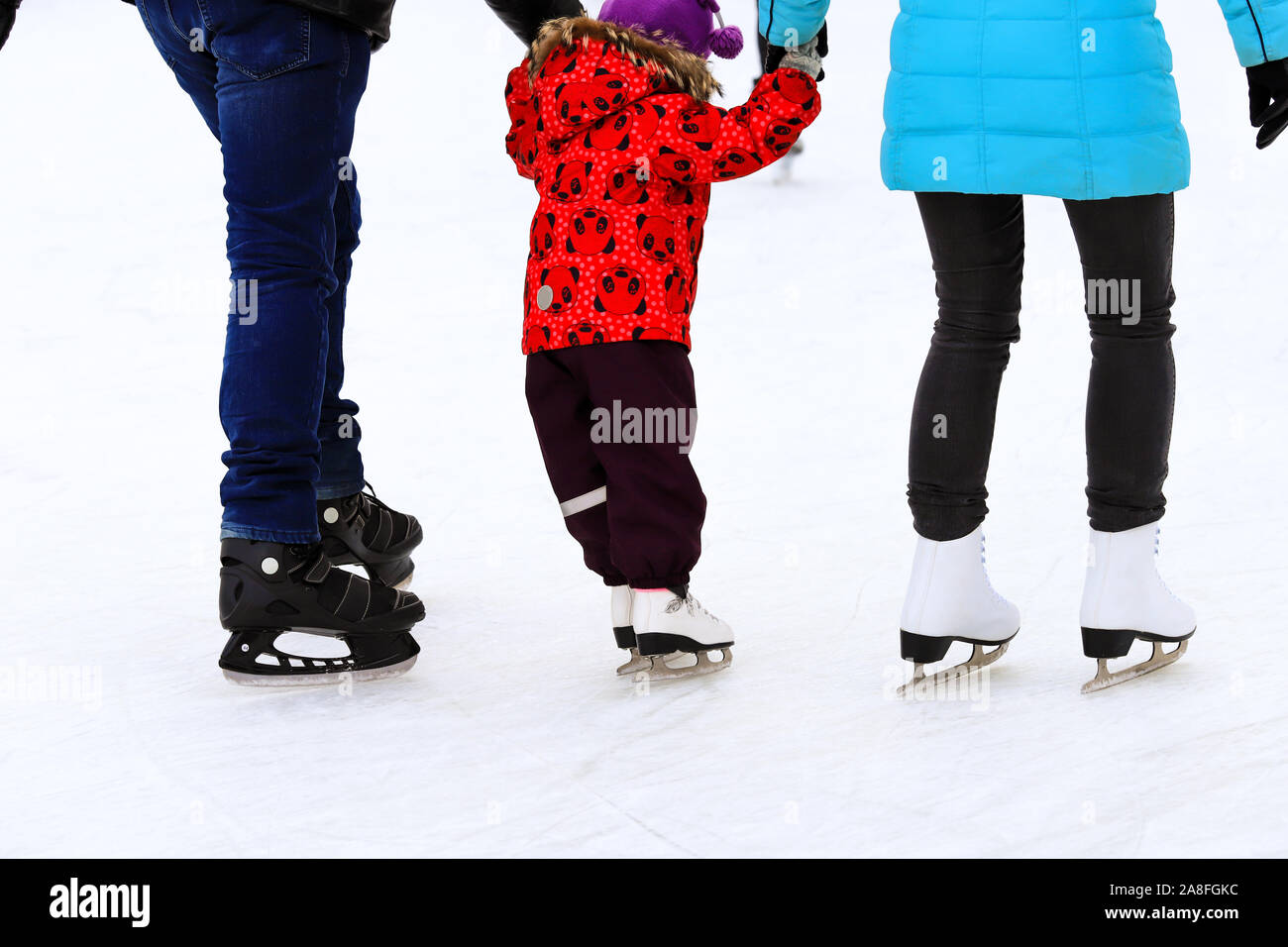 Little child skates with his parents at the ice rink in winter. A man ...