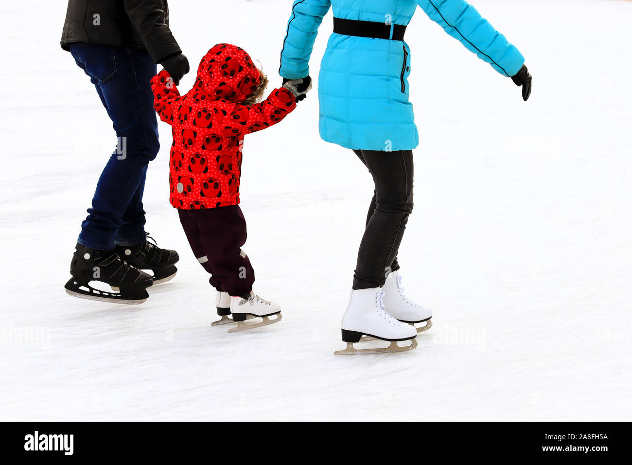 Little child skates with his parents at the ice rink in winter. A man ...